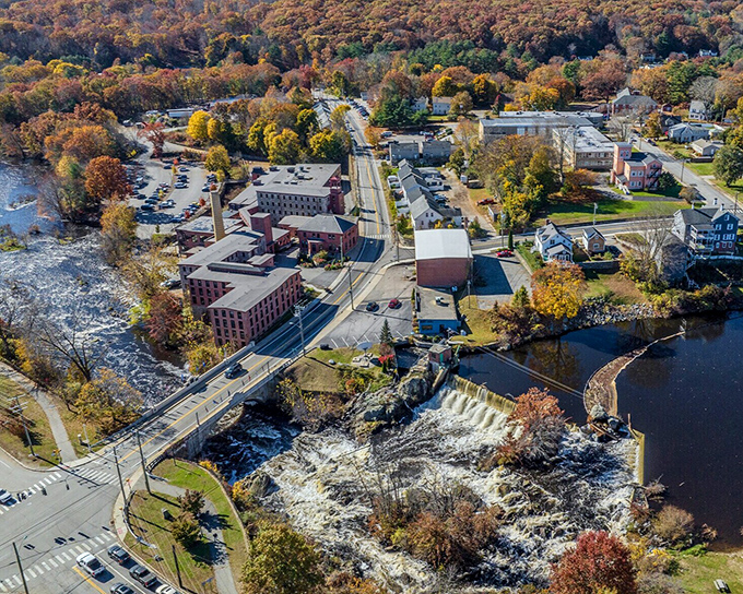 Historic mill buildings line the rushing waterfall where industrial heritage meets modern affordability in perfect harmony.