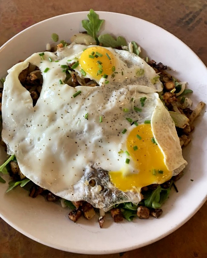 Eggs that break like the sunrise over a landscape of seasoned potatoes and savory ingredients – breakfast architecture at its finest.