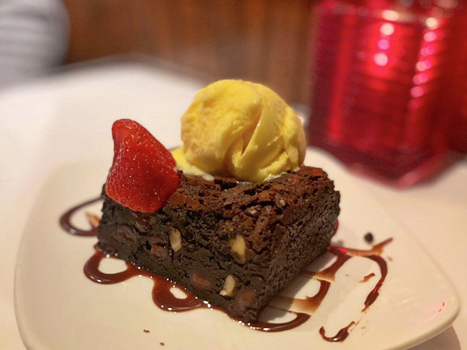 A brownie topped with gelato and chocolate drizzle, because apparently someone decided to weaponize happiness into dessert form.
