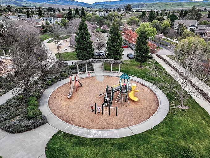 This playground sits like a perfect circle of childhood joy, surrounded by mountains that make jungle gyms seem quaint by comparison.