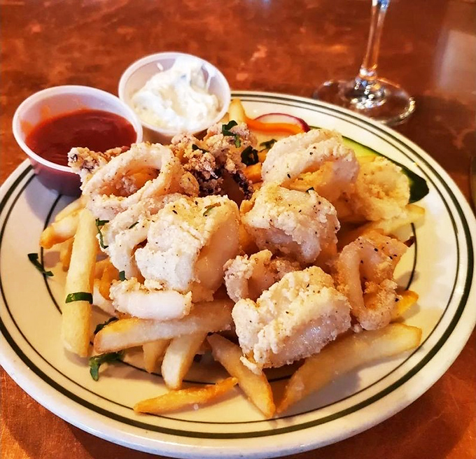 Crispy calamari perched atop golden fries—a tower of seafood excellence that disappears faster than your resolution to "just have a salad."