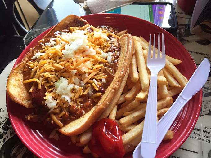 The chili dog arrives like a saucy celebrity on its red carpet plate, surrounded by an entourage of golden fries and wearing its cheese with confidence.