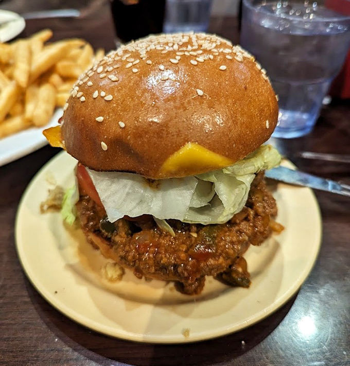A burger that requires both hands, a stack of napkins, and possibly a nap afterward. That sesame seed bun is barely containing the delicious chaos within.