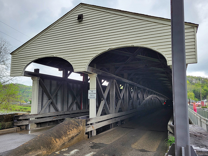 The bridge's entrance stands like a portal to the past, its wooden framework silhouetted dramatically against the light at the far end.