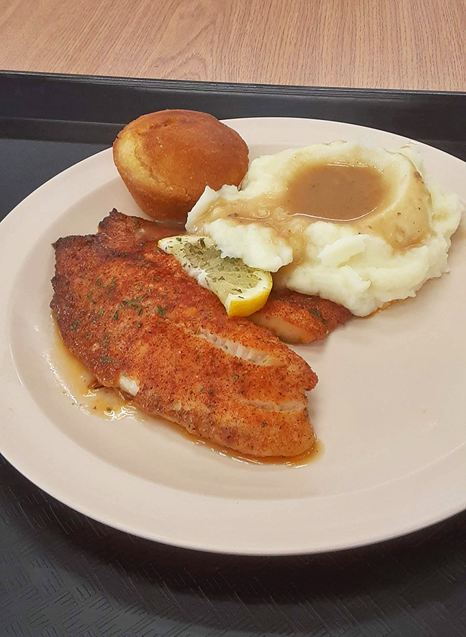 A perfectly seasoned fish fillet, mashed potatoes with gravy pools you could swim in, and a cornbread muffin that whispers, "Take your time, friend."