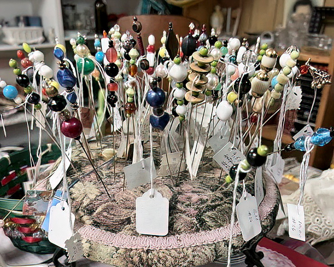 A pincushion forest blooms with vintage hat pins and sewing notions, each tiny treasure tagged and waiting for the right crafty collector.