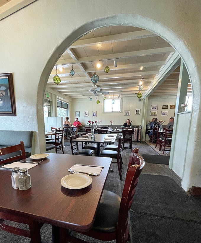 The arched doorway frames a dining room where culinary memories are made. Those colorful glass floats hanging from the ceiling? Pure coastal charm.
