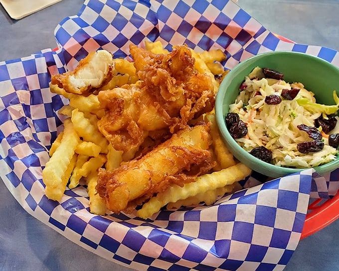 Golden-battered fish and crinkle-cut fries with coleslaw that actually deserves plate space. The checkered paper adds that touch of diner authenticity.