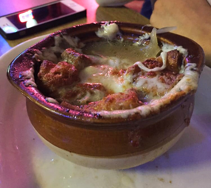 The French onion soup arrives bubbling with ambition, a molten cheese cap concealing savory treasures beneath its golden dome.