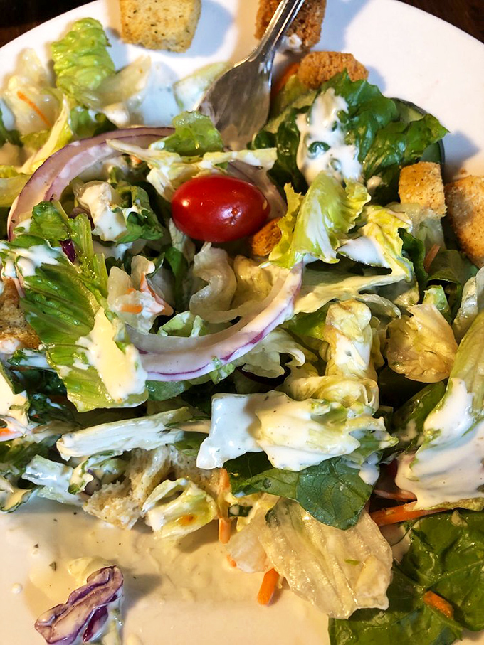 Even the salad looks happy to be here &ndash; crisp lettuce, veggies, and croutons playing nicely together under a light drizzle of house dressing.