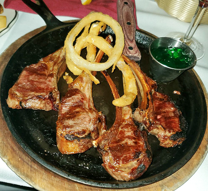 Lamb chops standing at attention like meaty soldiers, crowned with crispy onion rings and bearing perfect grill marks that whisper "order me."