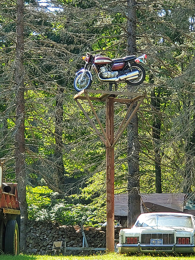 Defying gravity and common sense, this motorcycle perches atop its wooden tower like a mechanical bird surveying its junkyard kingdom.