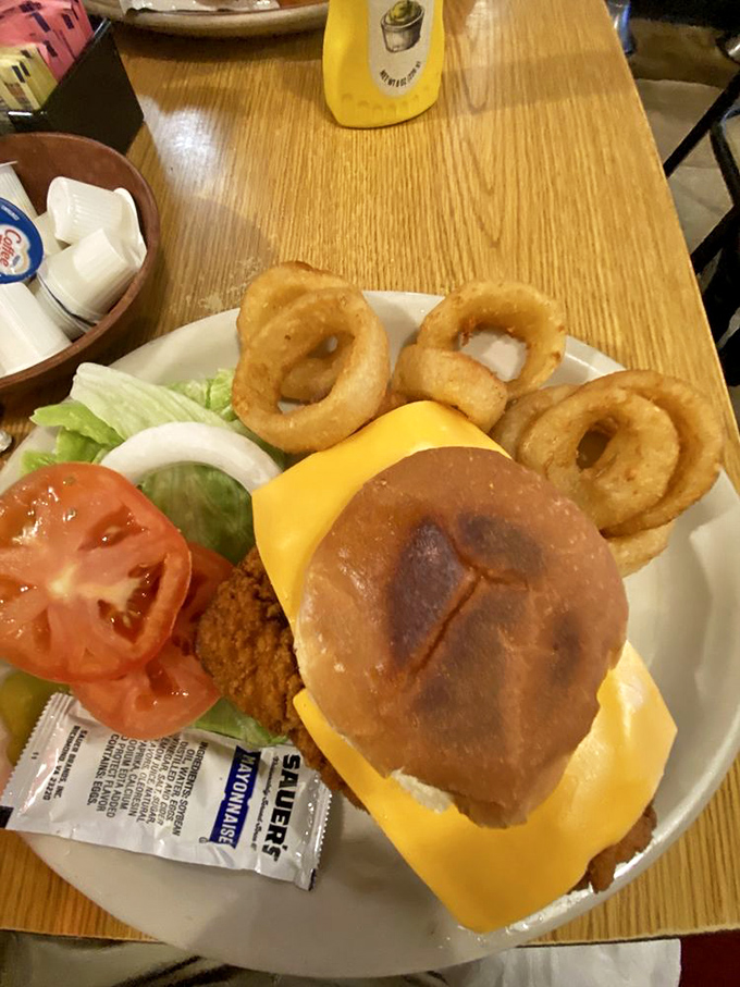 A pork tenderloin sandwich that refuses to be contained by its bun, surrounded by onion rings that could double as delicious golden halos.