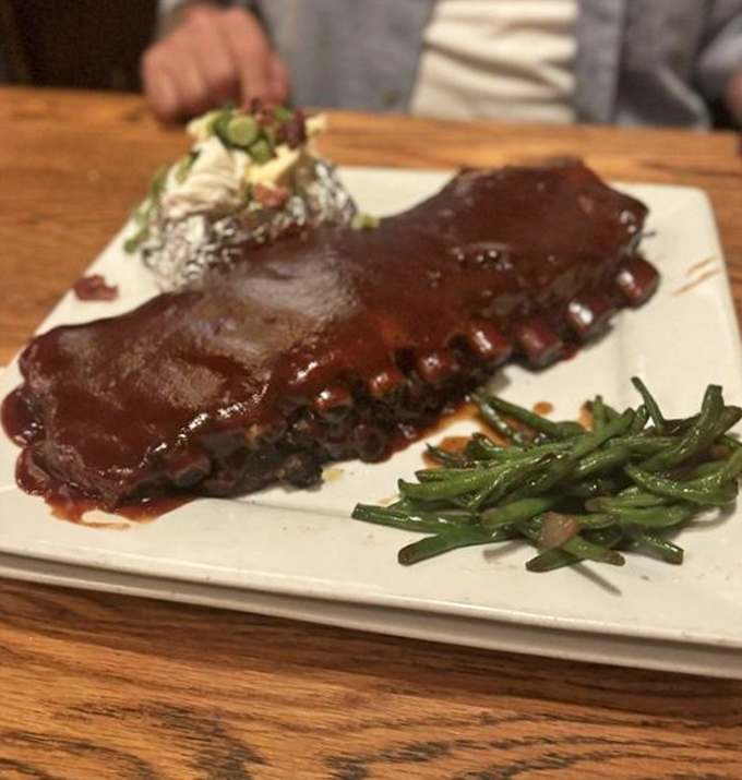 BBQ ribs glistening with sauce that would make a vegetarian question their life choices, served with a loaded baked potato and green beans.