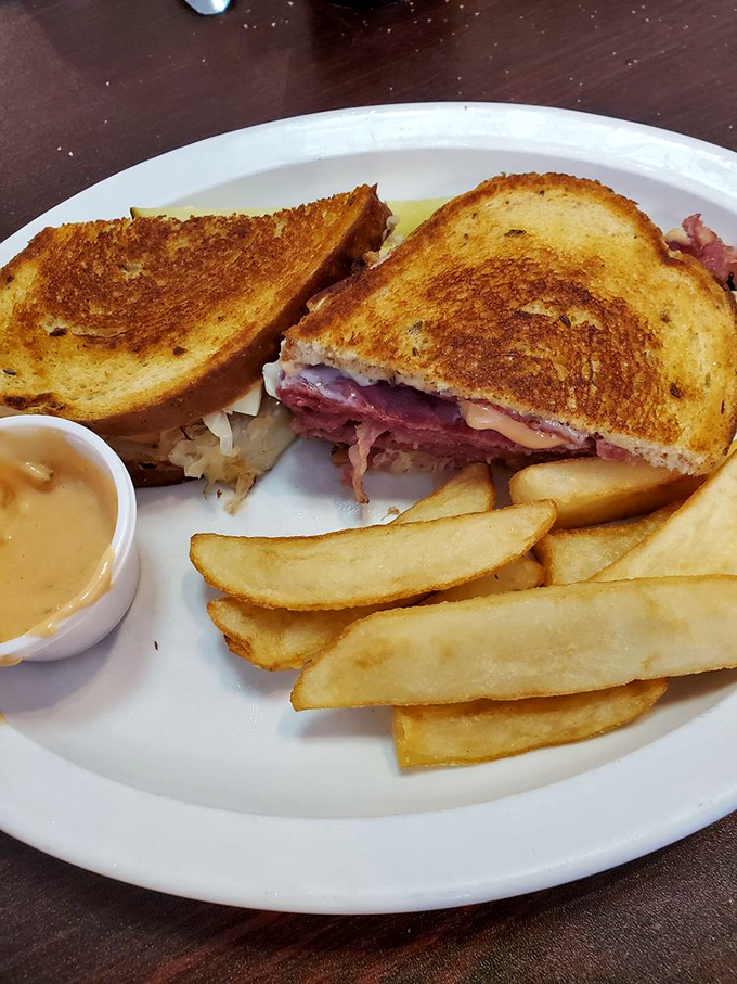 The Reuben reveals its secrets: layers of meat and sauerkraut peeking out from between perfectly grilled bread, with fries standing by for backup.