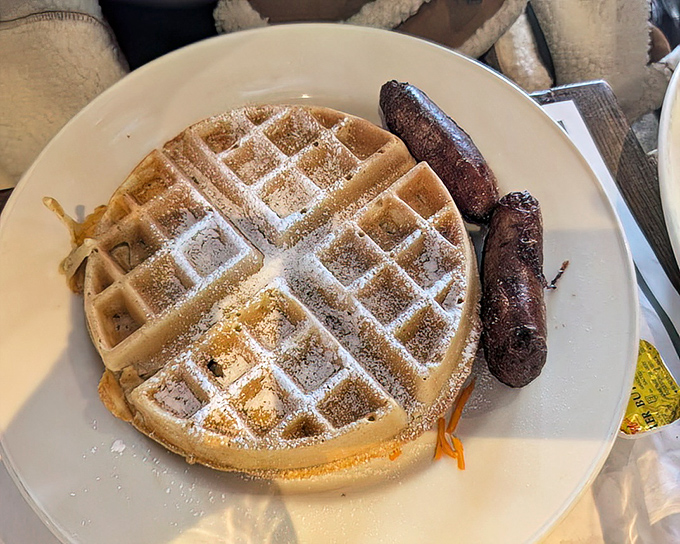 A waffle that's achieved perfect golden-brown status, flanked by sausages standing at attention like delicious sentinels guarding breakfast perfection.