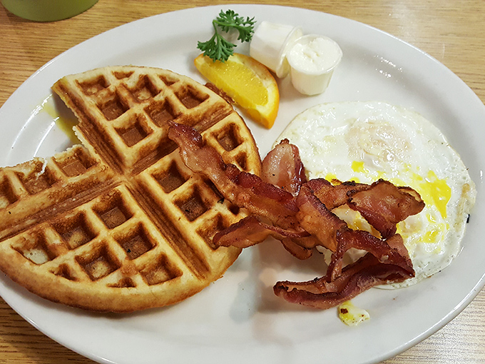 The Belgian waffle's perfect grid pattern creates little pools for maple syrup, while bacon and eggs wait patiently for their moment in the spotlight.