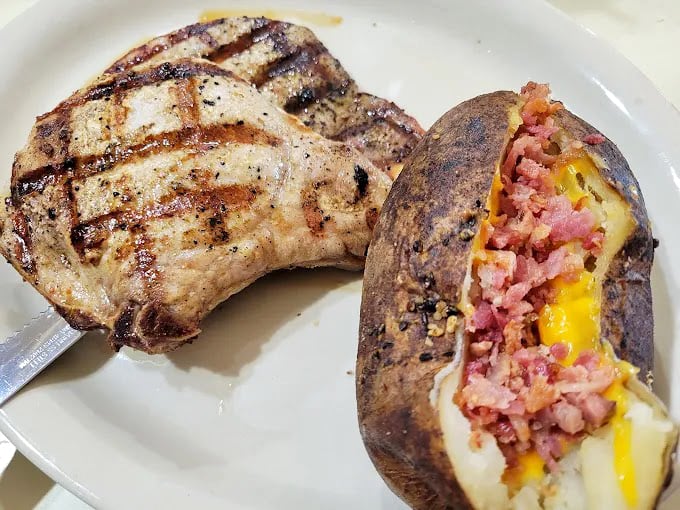 A perfectly grilled pork chop beside a loaded baked potato stuffed with ham and cheese&mdash;proof that simple food done right is culinary poetry.
