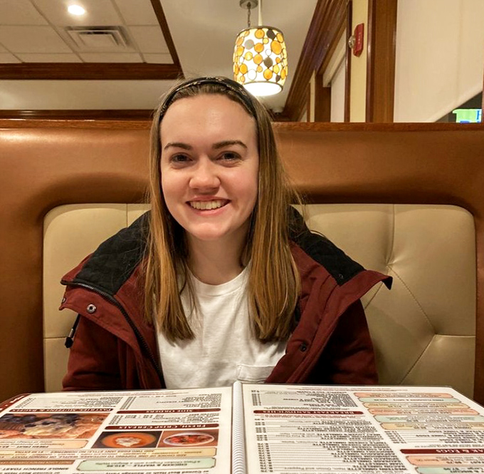 The warm glow of pendant lighting illuminates a patron enjoying the simple pleasure of perusing a diner menu&mdash;a moment of delicious anticipation.