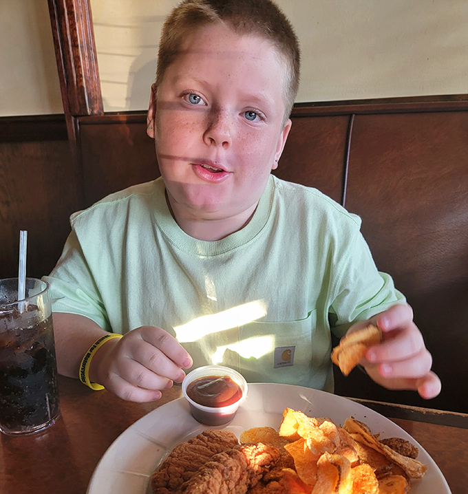 The image shows a young diner enjoying their meal at the restaurant. The genuine enjoyment on display speaks to the universal appeal of comfort food.