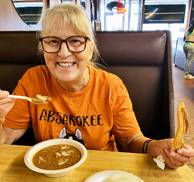 The joy of comfort food captured in one frame—a happy diner enjoying what appears to be soup and cornbread with the kind of smile that says "this beats fancy dining any day."