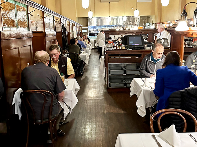 The narrow dining room buzzes with conversation while white-jacketed servers navigate the space with the precision of veteran sailors.