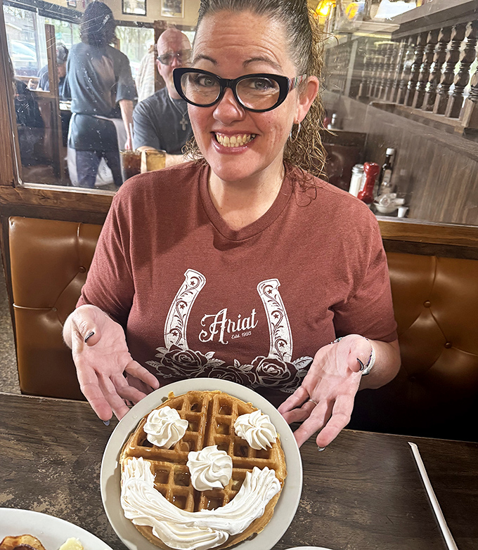 A happy diner showing off her waffle masterpiece – complete with whipped cream smiley face. Breakfast should always spark this much joy.