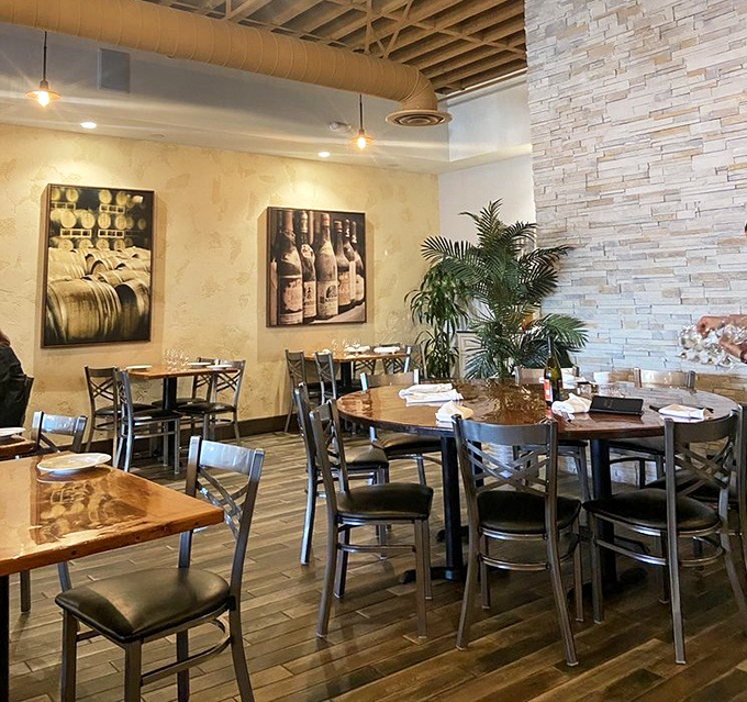 The dining area balances rustic charm with modern comfort, where wine-themed artwork reminds you that yes, you should definitely order a glass.