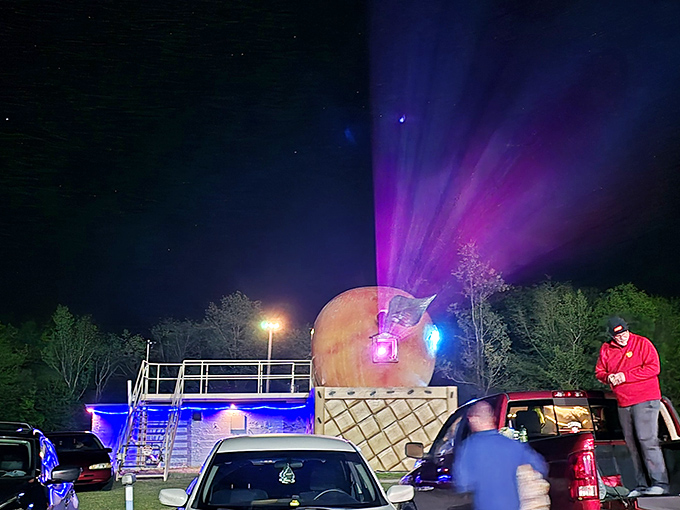 When darkness falls, the night sky becomes a canvas of stars while colorful lights illuminate the iconic peach, creating pure drive-in magic.