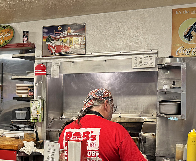 The grill master at work, wearing the Bob's red uniform—a conductor orchestrating a symphony of sizzles that's been playing since 1931.