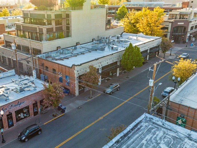 An aerial view of downtown Bend reveals a blend of historic brick storefronts and sleek modern buildings, framed by trees glowing in the Central Oregon sun.