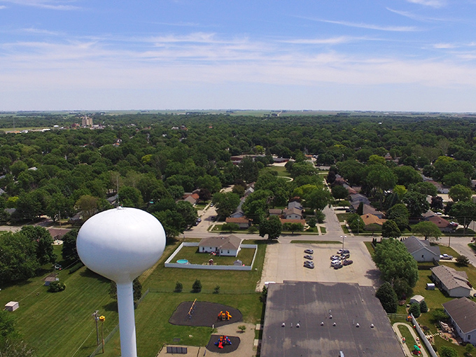Bird's eye bargains! Webster City spreads beneath its iconic water tower like a map of affordable living, where grocery bills are lighter than these wispy clouds.