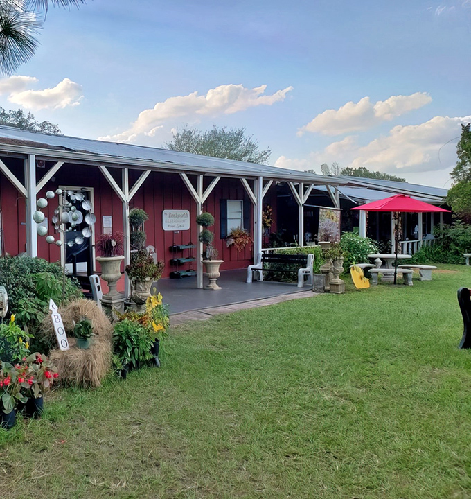 Shaded sanctuary awaits! The Back Porch's outdoor seating area offers a peaceful retreat under sprawling trees, where red umbrellas add pops of color to nature's canopy.