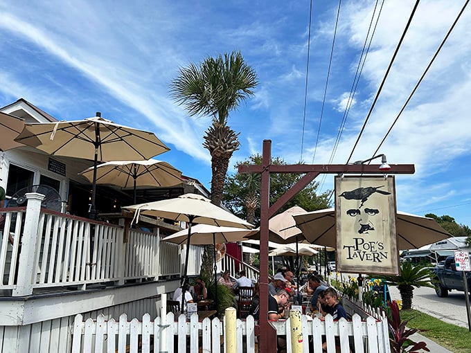 Poe's iconic white picket fence and palm-lined patio beckon like a literary oasis on Sullivan's Island. Those umbrellas aren't just for show—they're storytellers' canopies.