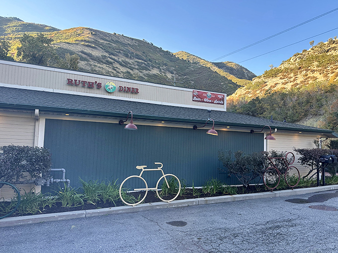 The iconic white exterior with "RUTH'S DINER" proudly displayed against the dramatic canyon backdrop makes cyclists regularly pause their uphill battle for a well-earned breakfast break.