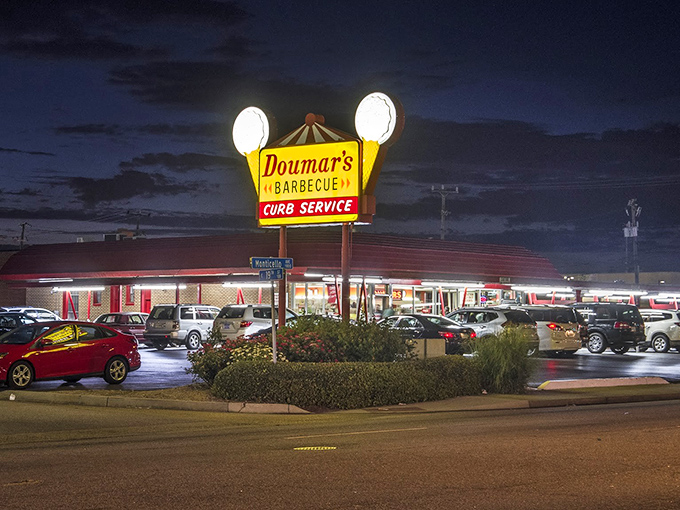 The iconic Doumar's sign glows like a beacon in the night, promising curb service and barbecue that's been drawing crowds since before color TV existed.
