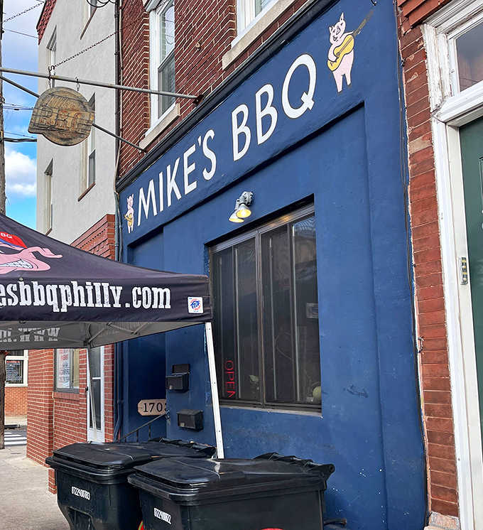 The blue storefront with its cartoon pig mascot stands like a beacon of smoky hope on this South Philly street. BBQ salvation awaits inside.