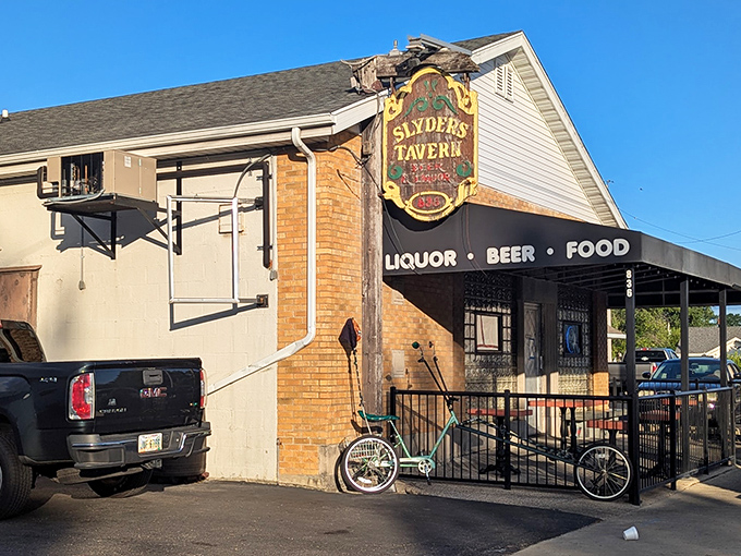 This photo shows the outside of a casual neighborhood tavern with a vintage sign, a small patio area, and a bike parked out front.