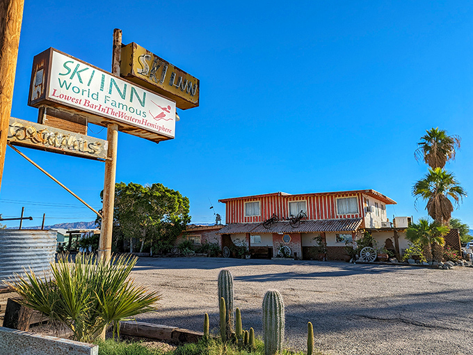 The Ski Inn's weathered sign proudly announces "World Famous Lowest Bar in Western Hemisphere" against a brilliant blue desert sky&mdash;a promise of cold drinks 223 feet below sea level.