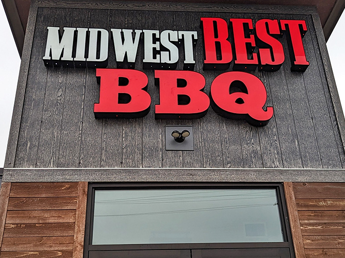 The bold red signage against rustic wood siding announces Midwest Best BBQ without pretense &ndash; like a smoke signal calling all hungry travelers home.