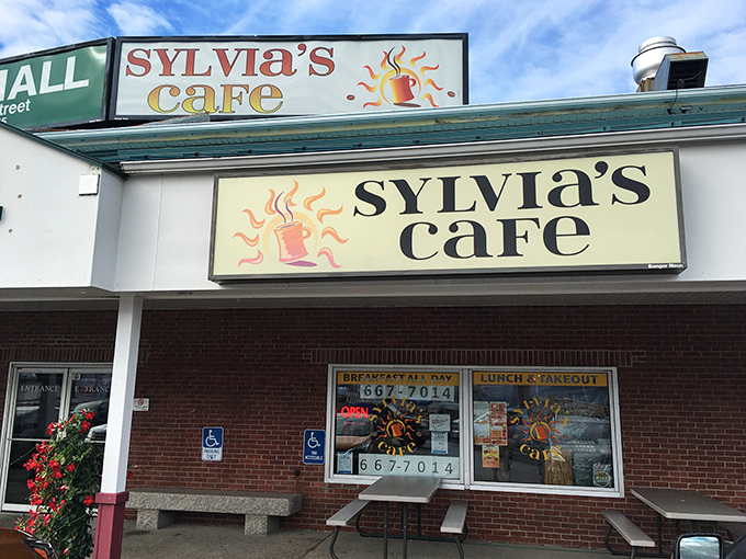 Sylvia's Cafe announces itself with cheerful confidence, that steaming coffee cup logo promising warmth inside those brick walls. No pretension, just breakfast all day and the promise of Maine comfort food.