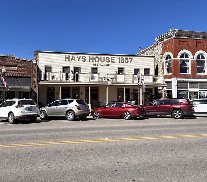 The historic facade of Hays House 1857 stands proudly against a Kansas sky, its balcony and columns whispering tales of Santa Fe Trail travelers who stopped here centuries ago.