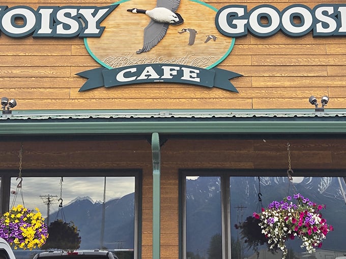 The iconic Noisy Goose sign welcomes hungry travelers with rustic charm, colorful hanging flower baskets, and the promise of mountain views that make breakfast taste even better.