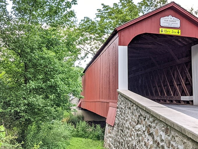 The classic red exterior of Van Sant Covered Bridge stands as a vibrant sentinel against Pennsylvania's lush greenery, a postcard-perfect scene from another era.