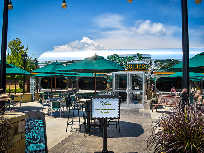 The outdoor patio at Roger's Diner beckons like an oasis for hungry travelers, complete with emerald umbrellas and a neon promise of comfort food ahead.