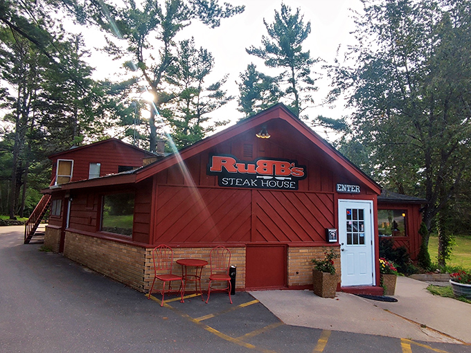Sunlight breaks through towering pines to welcome you to Rubb's, where the rustic red exterior promises steaks worth writing home about.