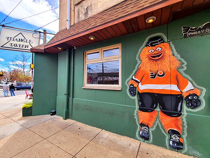 Gritty welcomes you to Triangle Tavern with his signature orange charm. This South Philly corner spot's green exterior promises comfort and character inside.