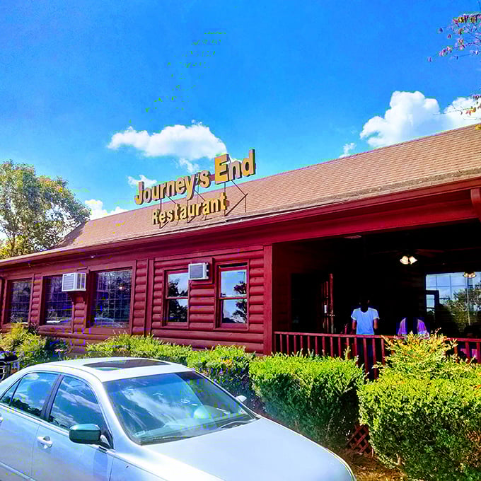 The iconic red log cabin exterior of Journey's End Restaurant stands out against the blue Georgia sky, promising comfort food treasures within its rustic walls.