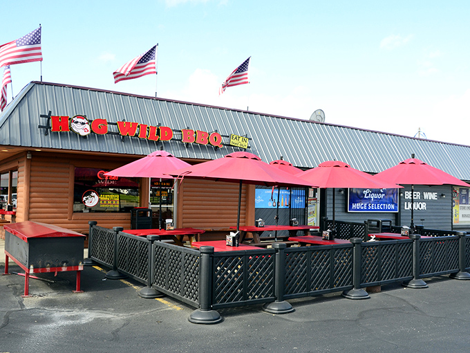 American flags flutter above this log cabin BBQ sanctuary, where red umbrellas invite you to linger over smoky treasures on warm Michigan days.