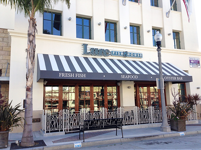 The blue and white striped awning of Lure Fish House beckons seafood lovers like a maritime flag signaling "fresh catch ahead!" The elegant ironwork adds a touch of coastal sophistication.